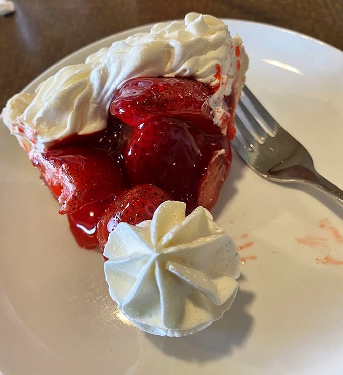 The famous strawberry pie makes its grand entrance—ruby red filling crowned with clouds of whipped cream. Dessert royalty that's earned every bit of its reputation.