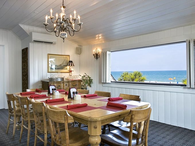The upstairs dining room combines elegance with coastal casualness—white-paneled walls, wooden tables, and that picture window framing the Atlantic like a living painting.
