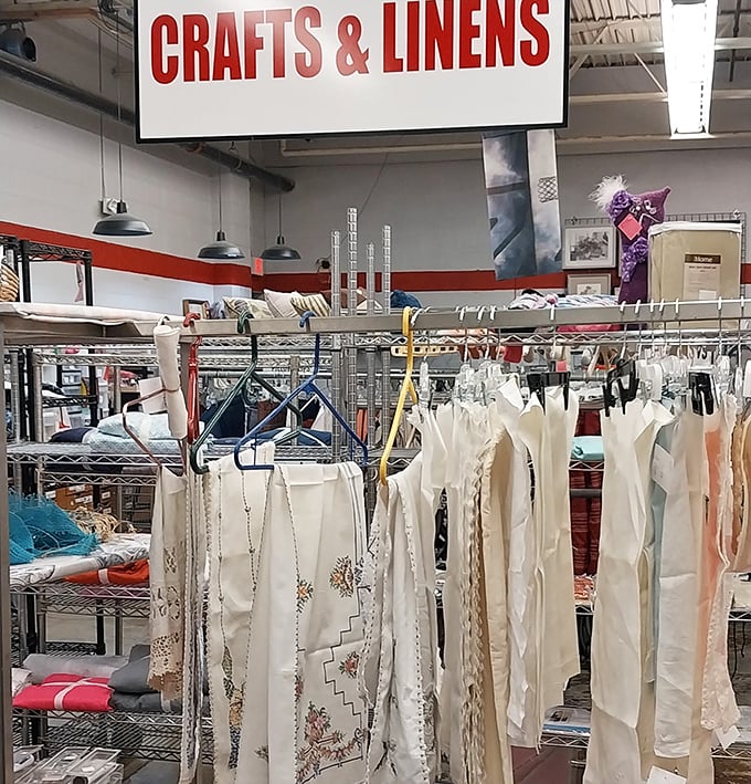 The crafts and linens section, where vintage tablecloths and handmade treasures hang like ghosts of dinner parties past, ready for resurrection at your next gathering.
