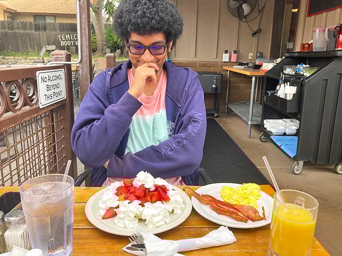A young diner contemplates breakfast choices while strawberries and whipped cream make a compelling argument for indulgence.