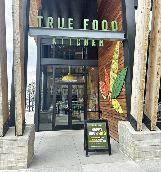The entrance beckons with wooden warmth and colorful leaf motifs. Even the Happy Hour sign promises guilt-free indulgence—now that's revolutionary.