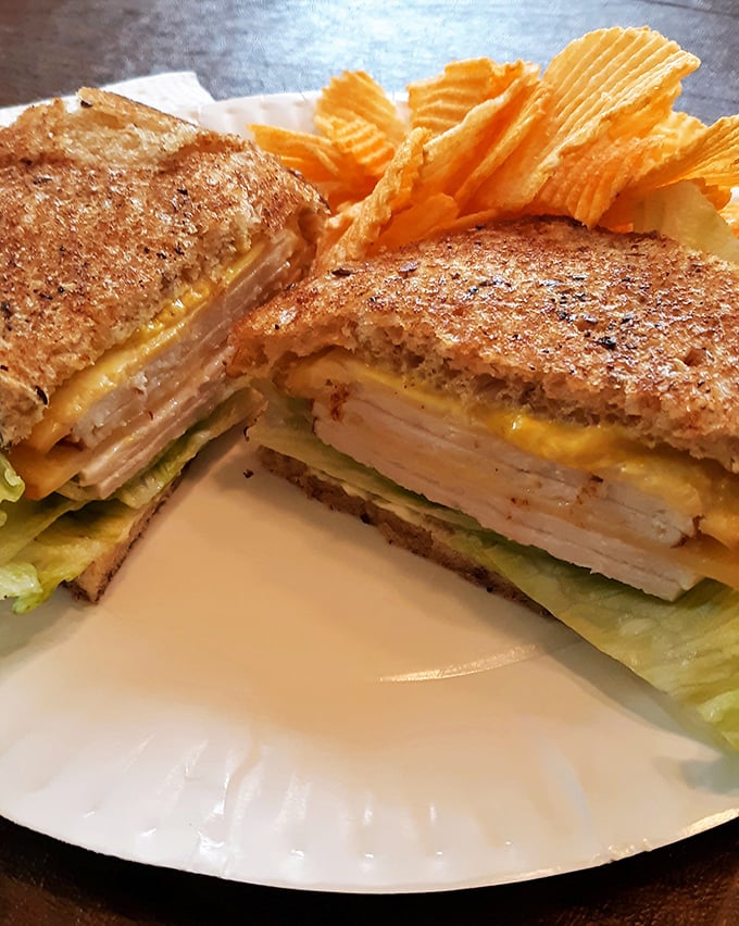 This sandwich isn't messing around—layers of turkey, cheese and veggies stacked with architectural precision and flanked by ridged chips.