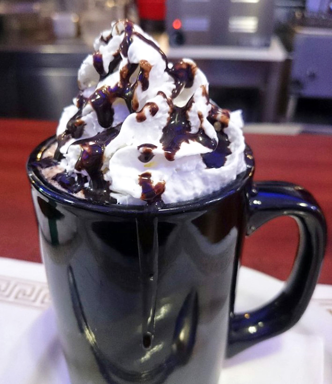 Hot chocolate elevated to an art form—whipped cream mountain drizzled with chocolate syrup. This isn't just a beverage; it's dessert with morning privileges.