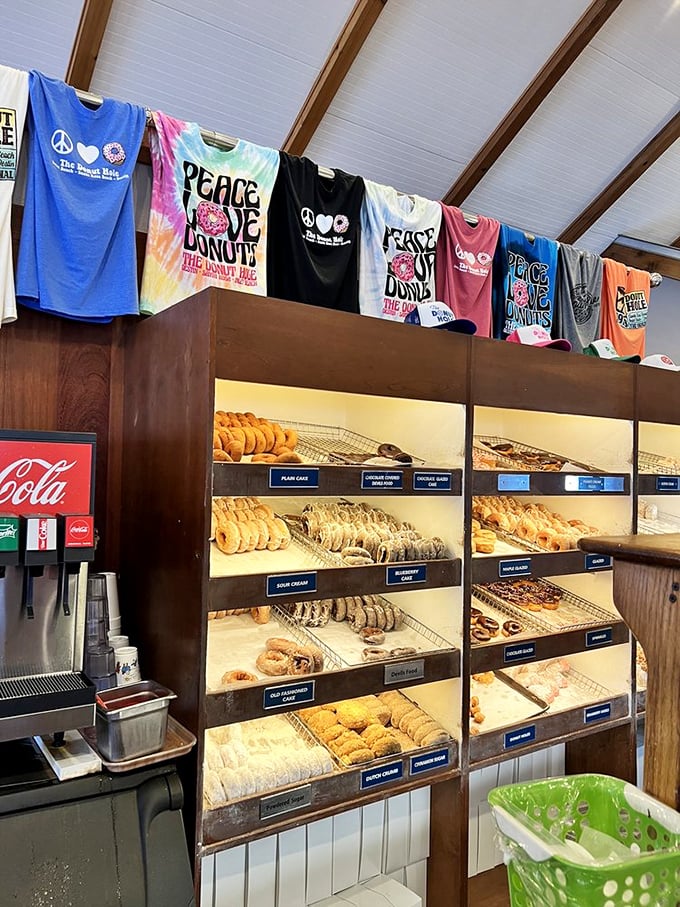 Peace, love, and donuts—the holy trinity of happiness. Those colorful shirts hanging above fresh-baked treasures perfectly capture the Donut Hole philosophy.