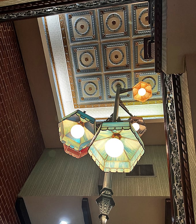 The ornate tin ceiling and colorful pendant lights create an atmosphere that whispers, "Your Instagram feed can wait—dinner is served."