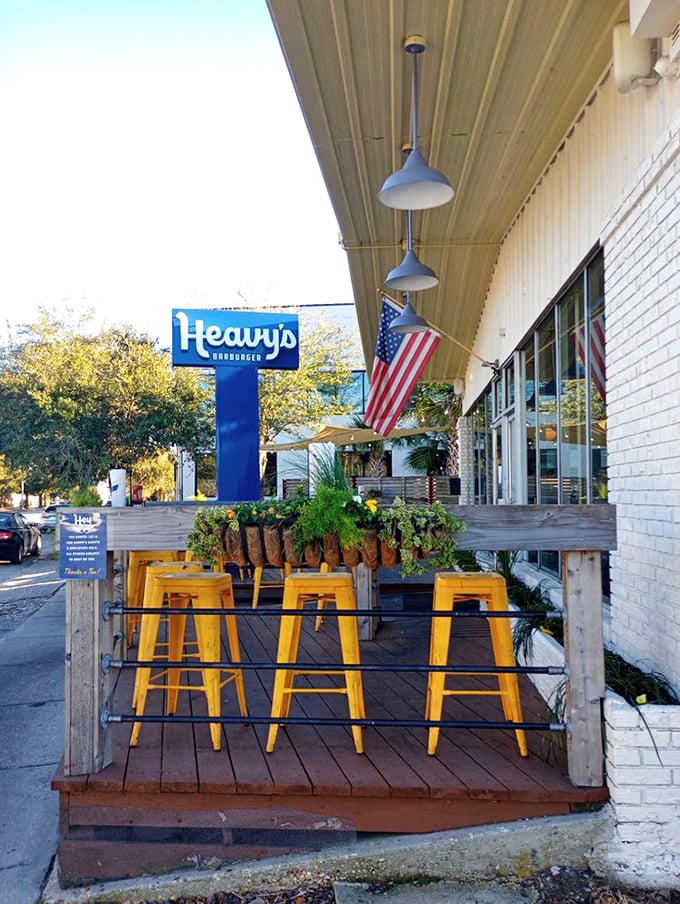 Yellow bar stools pop against the wooden deck, creating a sunny perch for outdoor dining. American flags flutter overhead—because patriotism pairs well with patties.
