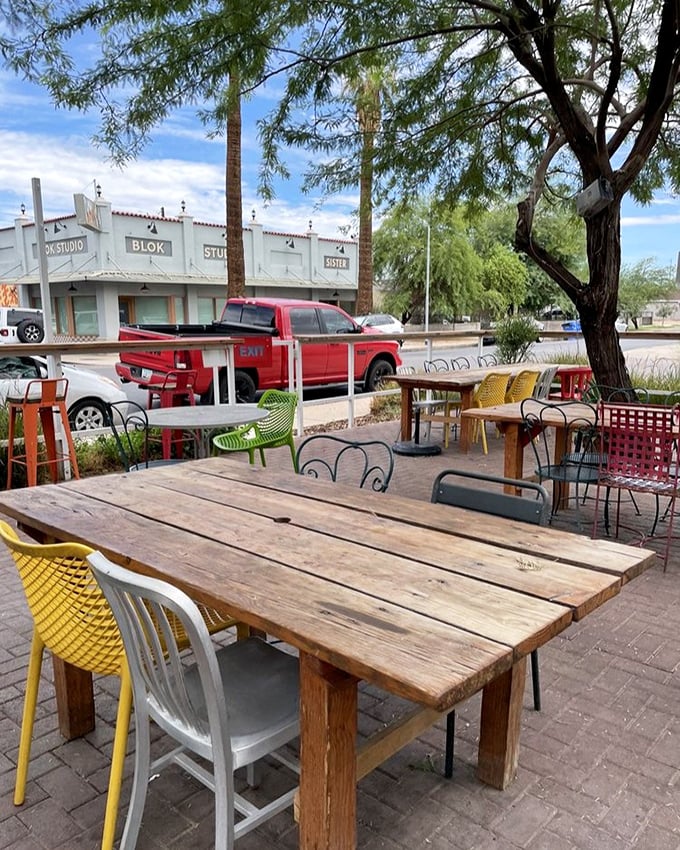 Mismatched chairs in cheerful colors surround rustic wooden tables—the outdoor dining equivalent of a warm hug from an eccentric aunt.