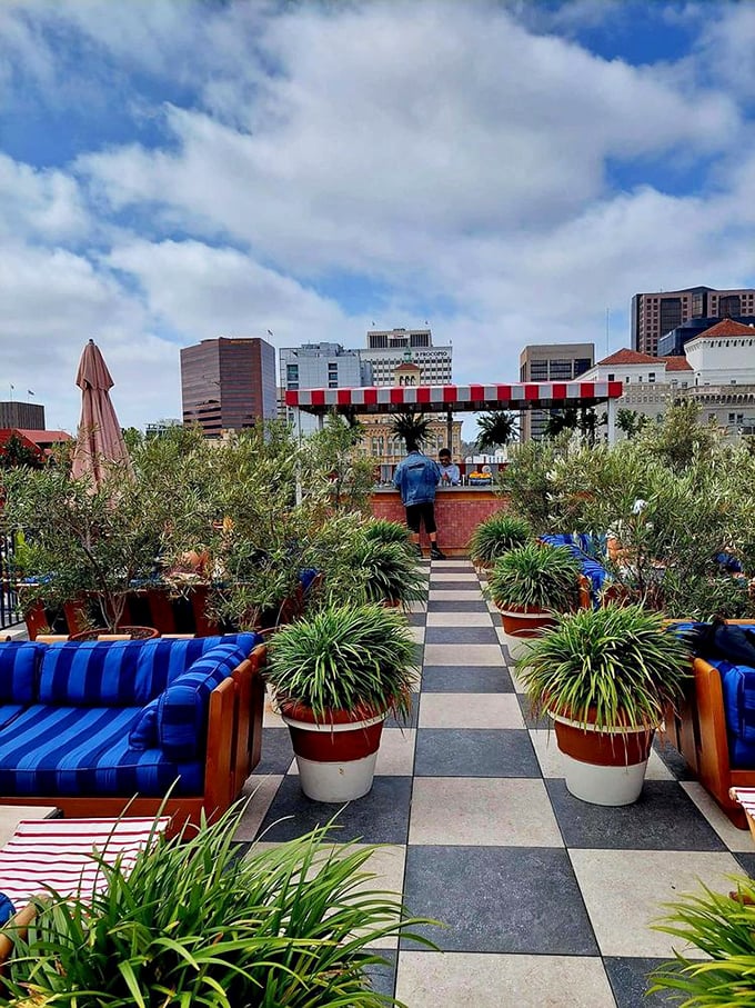 The outdoor patio offers an urban oasis with its checkerboard floors and lush greenery. Blue cushions pop against terracotta planters—California sunshine meets French sensibility.