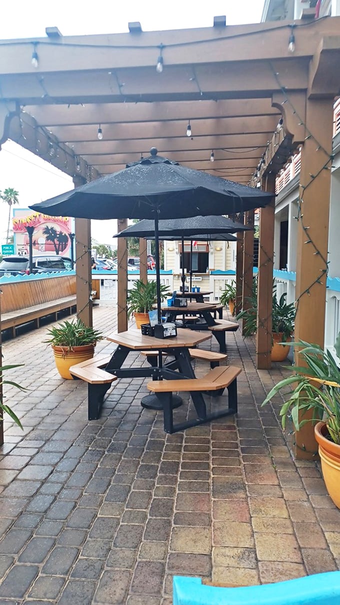 The outdoor patio offers string lights, umbrella-shaded tables, and potted palms – a casual oasis where beach vibes meet culinary delights.