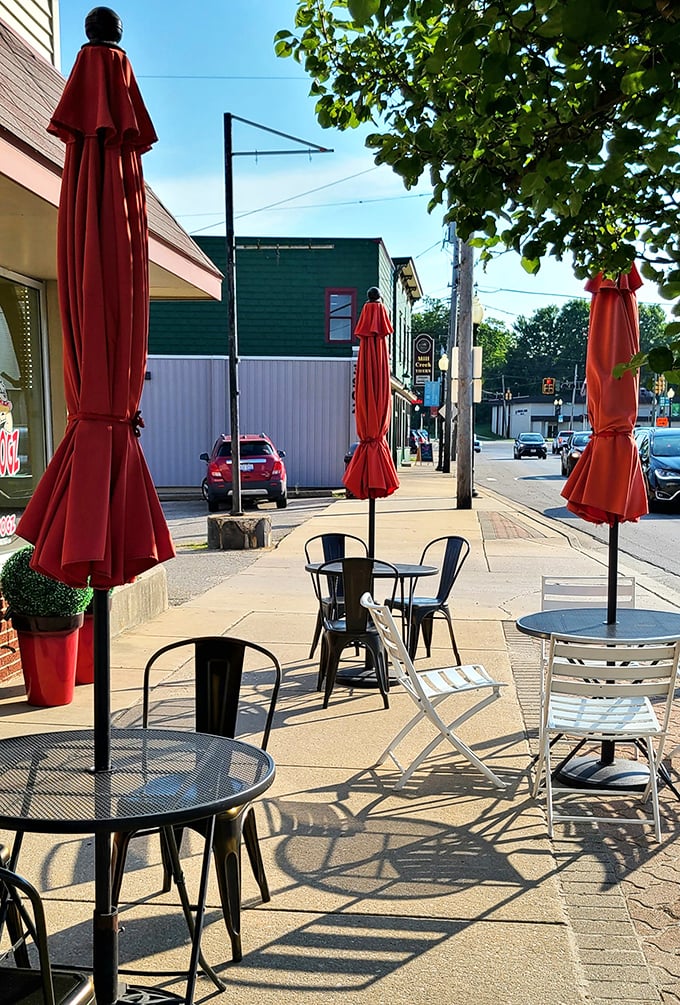 Red umbrellas provide shade for outdoor diners savoring gourmet hot dogs in perfect comfort.