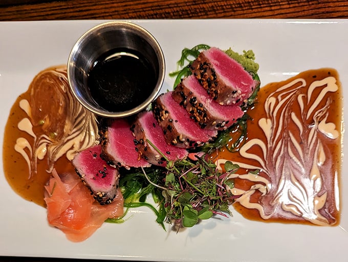 The seared ahi tuna arrives like edible art—ruby-red slices fanned across the plate with sauces creating a Jackson Pollock-worthy backdrop that's almost too beautiful to eat. Almost.