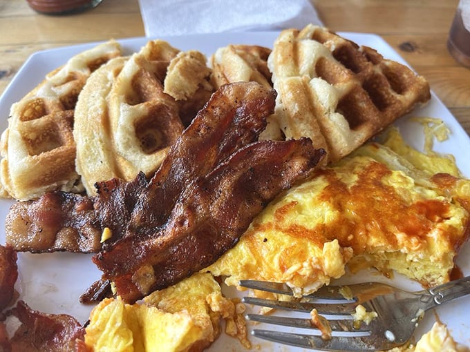The breakfast trinity—golden waffles, crispy bacon, and sunny eggs—executed with the kind of precision that turns morning grumps into believers.