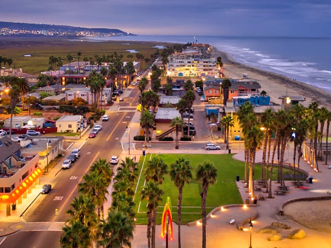 An evening aerial view captures Imperial Beach’s charming streets, glowing lights, palm trees, and the endless Pacific shoreline stretching beyond.