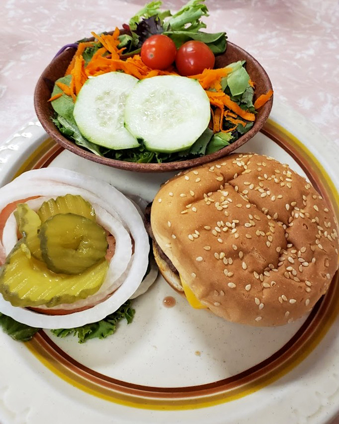 The classic burger setup – sesame seed bun, melted cheese, fresh veggies, and pickles on the side for those who understand that condiment control is personal.