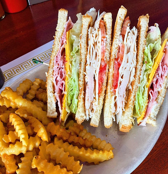 The club sandwich—architectural marvel of turkey, bacon, and vegetables between perfectly toasted bread. Those crinkle fries aren't just along for the ride—they're essential co-stars.
