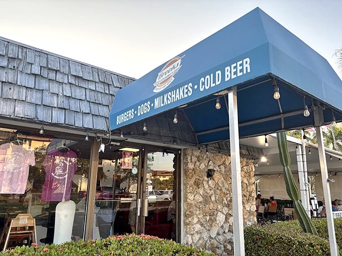 The blue awning proudly announces "BURGERS • DOGS • MILKSHAKES • COLD BEER"—four horsemen of the appetite apocalypse.