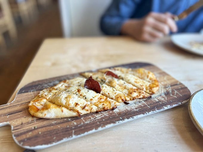 This flatbread isn't just food—it's edible architecture. Perfectly charred, topped with cheese and what appears to be prosciutto, it's hand-held happiness.