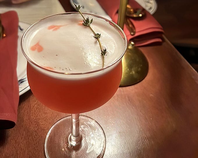 A pink cocktail garnished with fresh herbs that looks like it belongs in the hands of someone far cooler than you – until you order one yourself.