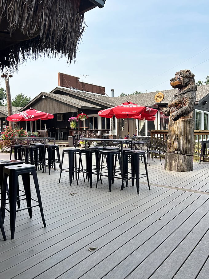That wooden bear statue isn't just decoration—it's the unofficial greeter to Jake's outdoor paradise where summer memories are made one lakeside meal at a time.