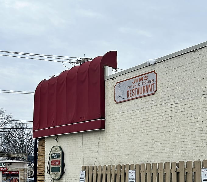 The weathered sign on the white brick exterior tells you everything and nothing—this isn't just Jim's Open Kitchen, it's a community institution serving memories with every meal. 