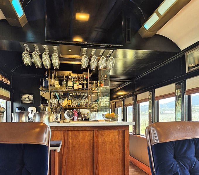 The train's bar car—where hanging glassware catches the light like crystal chandeliers and every bottle tells a story worth hearing.