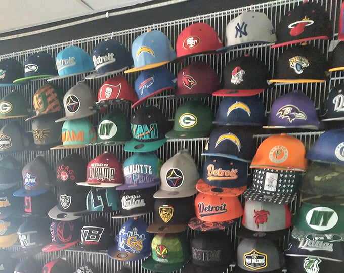Sports fans unite! This wall of team caps represents fierce rivalries hanging peacefully side by side—until they're worn out into the world.