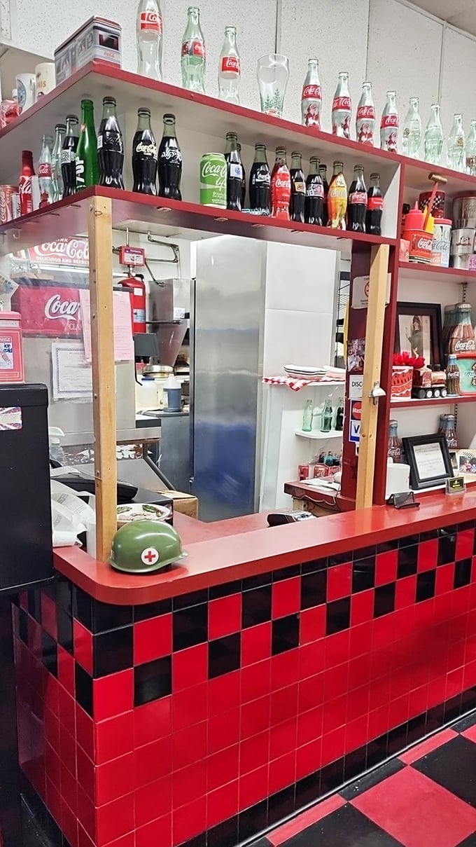 The Coca-Cola collection above the pass-through window proves this place takes its Americana seriously—right down to the red and black checkered counter.