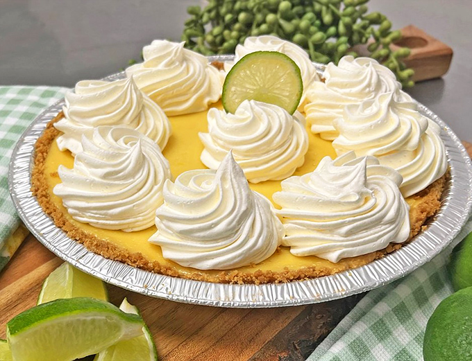 The key lime pie in all its glory—sunshine-yellow filling, cloud-like whipped cream peaks, and that lime slice winking at you like it knows something.