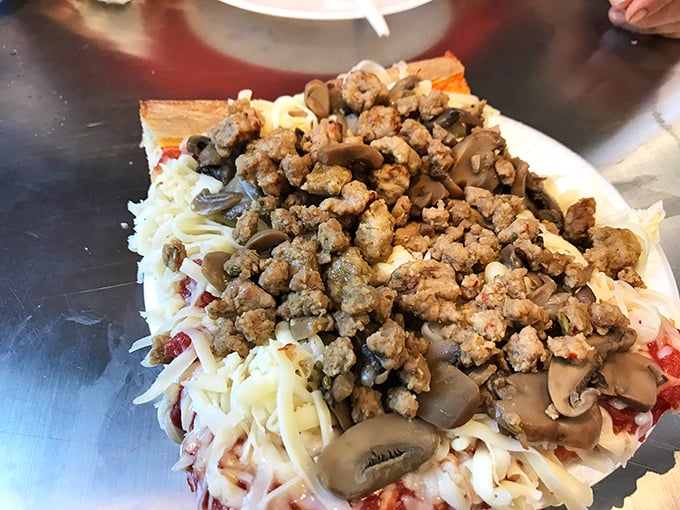 A close-up of pizza perfection – sausage, mushrooms, and that signature cold cheese creating a topographical map of flavor that needs no explanation.