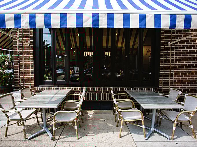The outdoor seating area waits patiently under blue and white stripes – like a Parisian café that somehow wandered into Philadelphia and decided to stay.