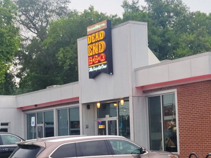 That neon sign beckons like a lighthouse for the hungry, promising safe harbor from mediocre meals and sad sandwiches.
