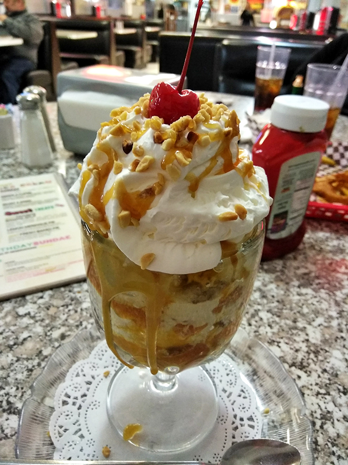 A sundae that defies gravity and good sense—whipped cream mountain, caramel rivers, and that cherry on top saying "you deserve this."