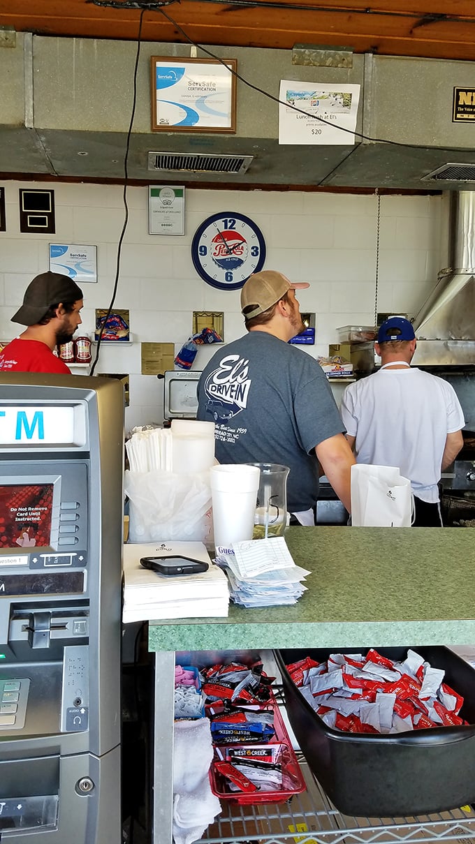 Behind the counter at El's, where burger magic happens. That Pepsi clock has witnessed decades of delicious decisions being made.
