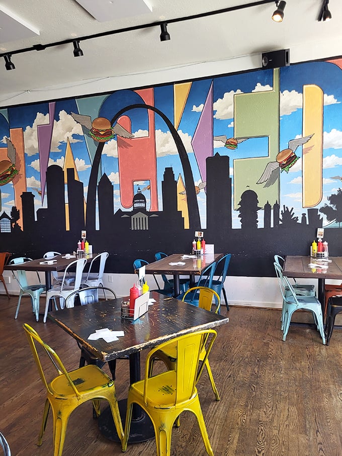 Colorful metal chairs pop against the whimsical St. Louis skyline mural where flying burgers soar past the Gateway Arch—dinner and a show!