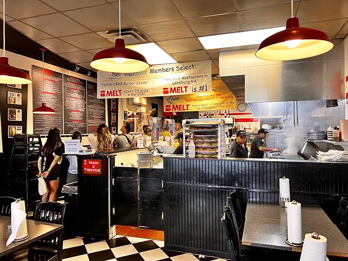 The open kitchen design lets you witness the burger alchemy in progress. Red pendant lights cast a warm glow over the checkered floor – burger joint perfection.
