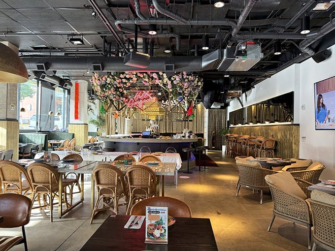 Floral installations cascade from the ceiling like a Bangkok market in full bloom, creating an atmosphere that feeds your Instagram before the food feeds you.