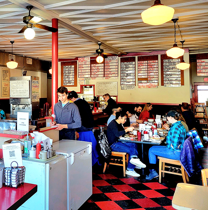 The interior is a symphony of organized chaos—red and black checkerboard floors, handwritten menu boards, and the constant buzz of satisfaction.