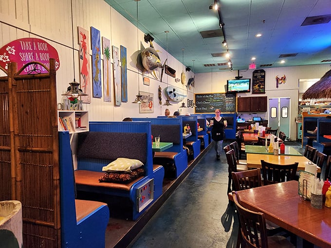 Beach vibes meet burger bliss inside with vibrant blue booths, local art, and a "Take a Book, Share a Book" shelf that says "stay awhile, we're neighbors here."