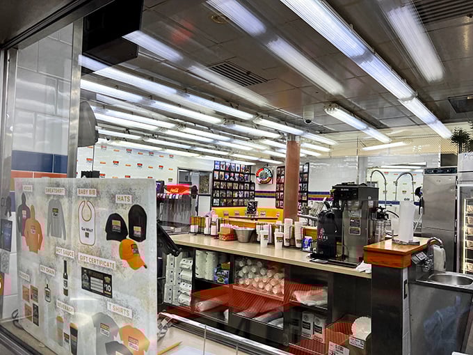 Behind the counter, where cheesesteak magic happens. The pristine workspace and branded merchandise wall hint at decades of sandwich-making precision.