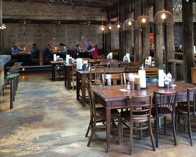 The dining room where barbecue dreams come true – wooden communal tables bathed in warm light from industrial fixtures, all designed for serious meat contemplation.