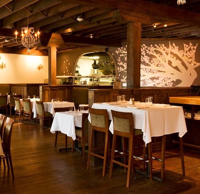 Exposed wooden beams, white tablecloths, and that stunning tree silhouette—Orsay's dining room manages to be both sophisticated and comfortable, like wearing a tuxedo with slippers.