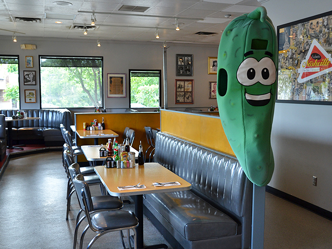 Meet the unofficial greeter of Noshville – a giant pickle mascot who never complains about standing all day. The classic diner booths behind him have witnessed countless food epiphanies.