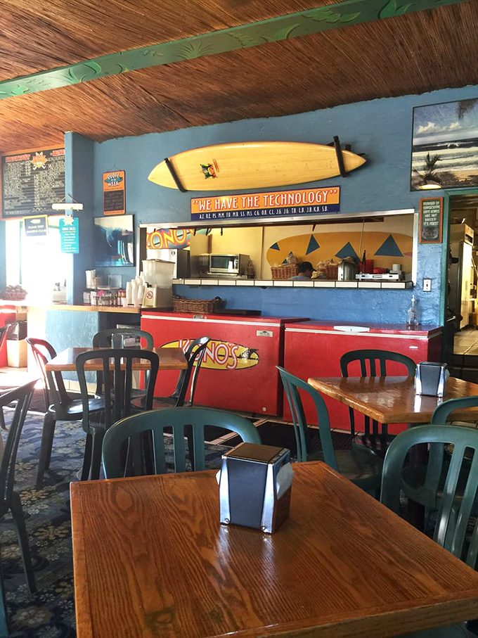 Surfboards don't lie—this interior screams "California beach culture" with its wooden tables, blue walls, and that cheeky "We Have The Technology" sign above the kitchen.
