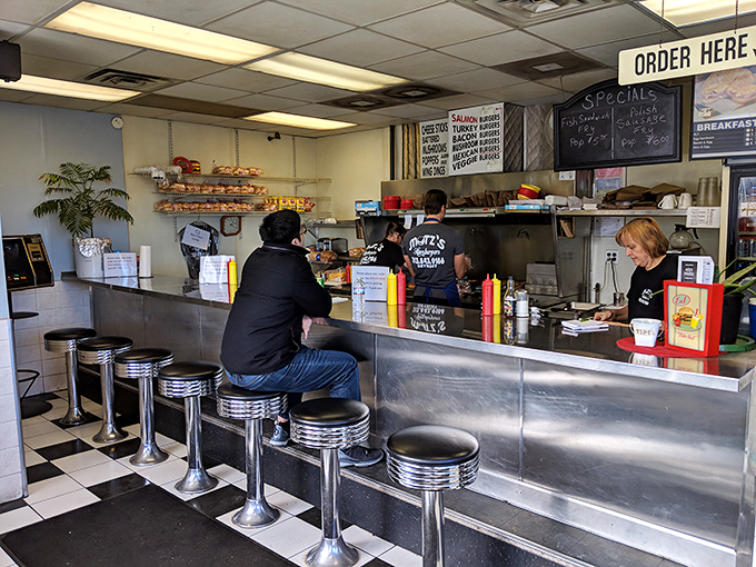 Classic Americana at its finest—chrome counter stools, checkered floor, and a front-row seat to the burger ballet. This is dinner theater for food lovers.