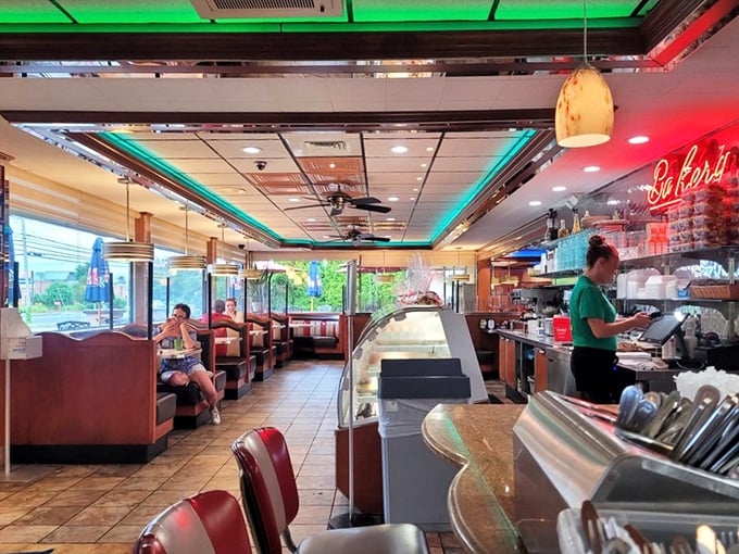 Classic red vinyl booths under neon lighting create that timeless diner atmosphere where conversations flow as freely as the coffee.
