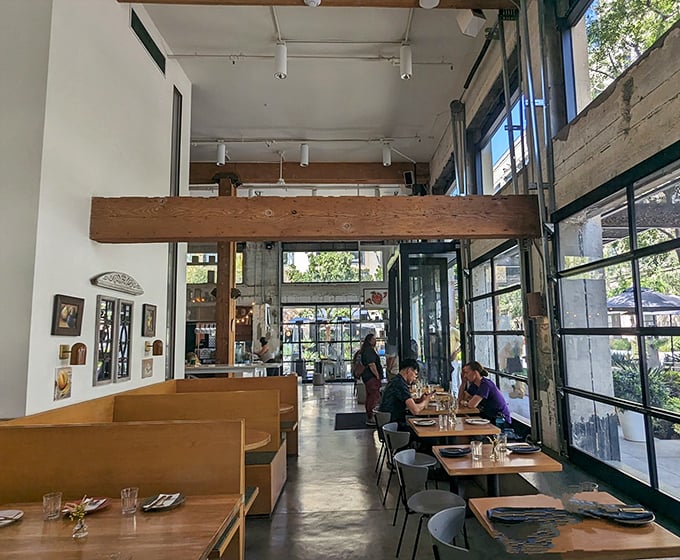 Inside, sunlight streams through floor-to-ceiling windows, illuminating wooden beams and minimalist furnishings—proof that great pizza needs no elaborate backdrop.