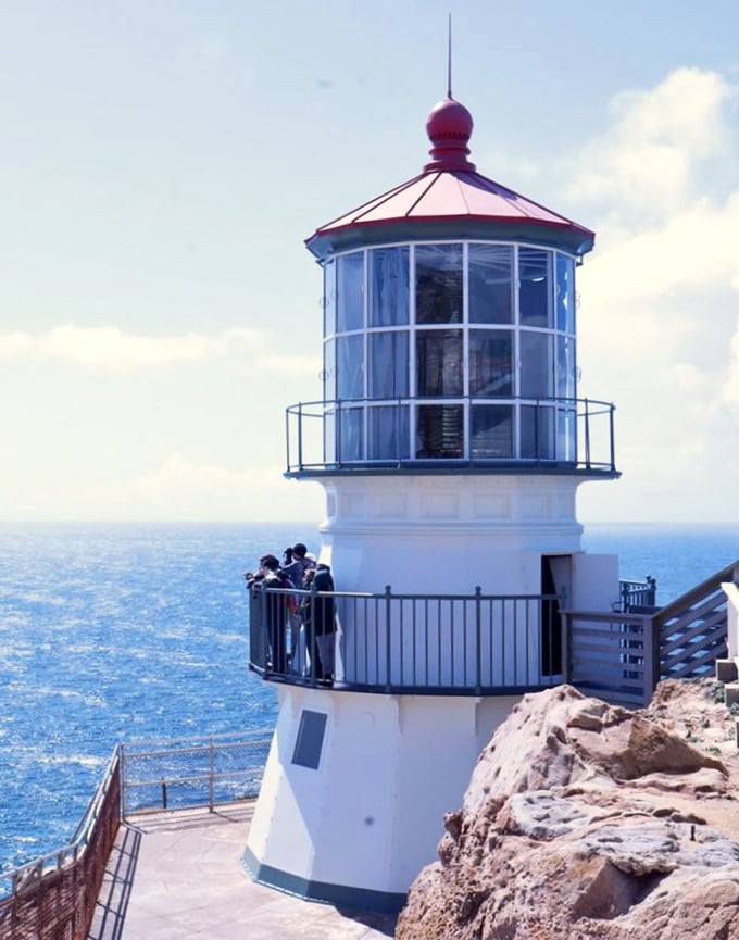 Maritime elegance in white and red, the lighthouse tower stands sentinel against the endless blue, a postcard moment that's earned every step down.