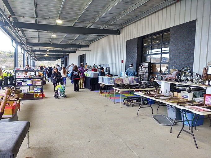 Under a long covered walkway, vendors display antiques and collectibles while shoppers hunt for hidden treasures at a bustling flea market.