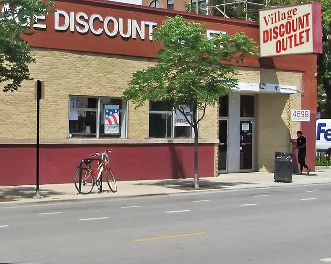 The iconic Village Discount Outlet sign beckons thrifty shoppers to discover their next favorite outfit inside.
