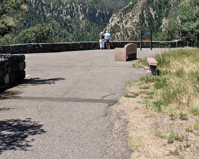 Visitors pause at the stone-walled viewpoint, contemplating the vastness below – a moment where smartphones are finally forgotten in favor of actual, jaw-dropping reality.